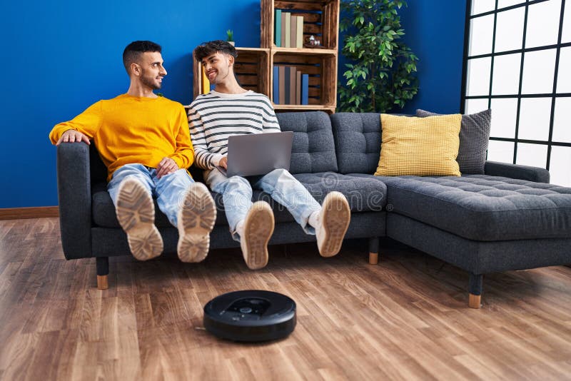 Two Man Couple Using Laptop and Vacuum Cleaner Robot Sitting on Sofa at ...