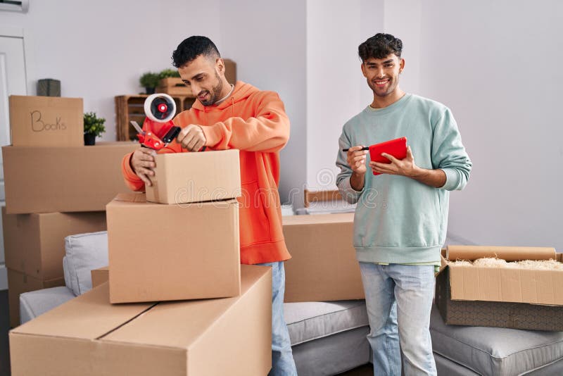 Two Man Couple Using Touchpad Packing Cardboard Box at New Home Stock ...