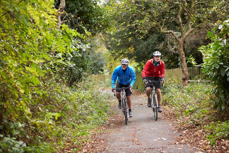 Two Mature Male Cyclists Riding Bikes Along Path Stock Photo - Image of ...