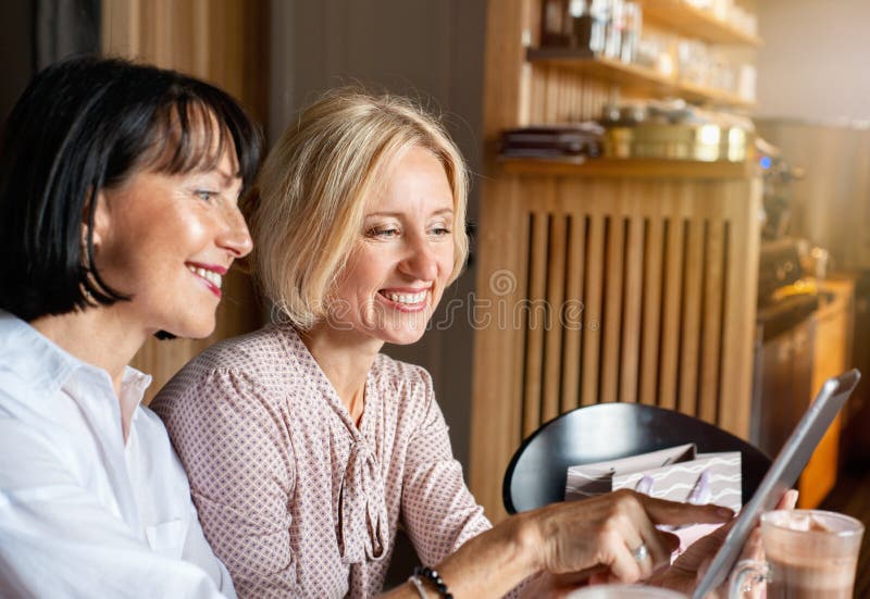 Two Mature Women Chatting And Using The Tablet Device While Having