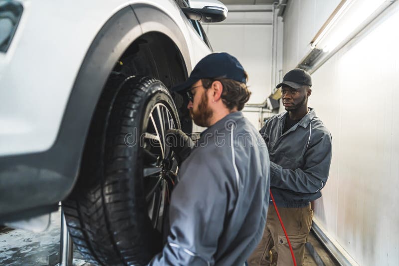 Two Mechanics at Work. One Changing a Tyre, Another Looking at Thr ...