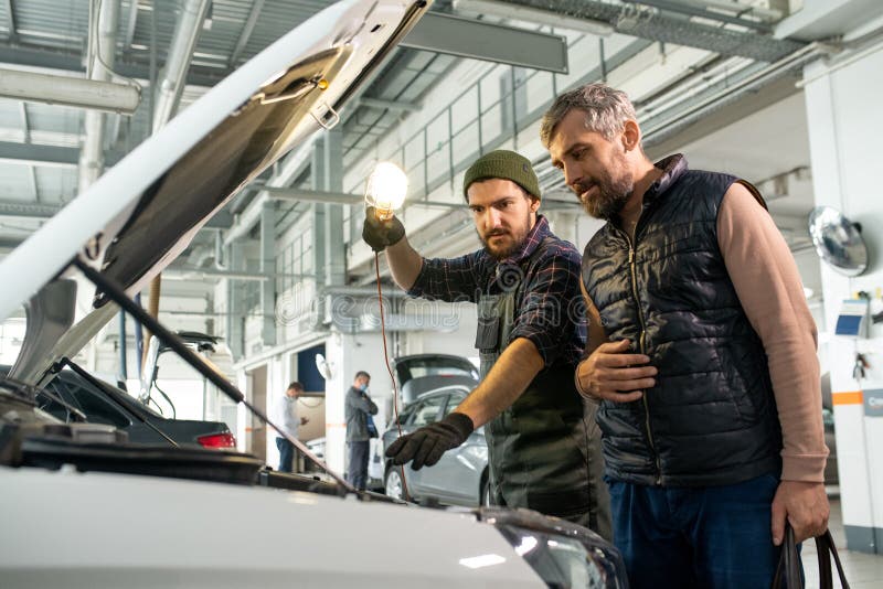 Two Men Bending Over Car Engine while Technician Pointing at One of Its ...