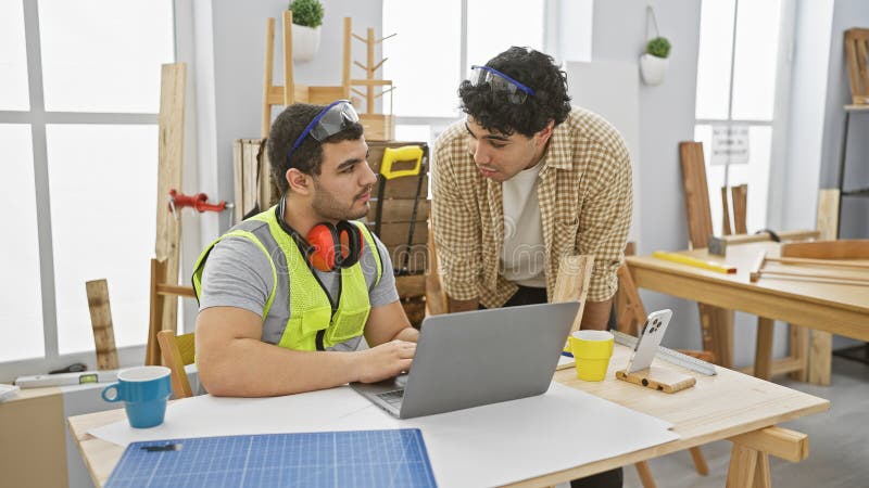 Two Men Discussing Work on a Laptop in a Bright Carpentry Workshop with ...