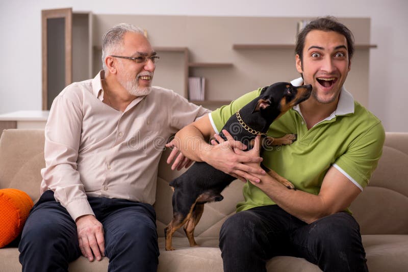 Two men with dog at home stock photo. Image of friend - 214534018