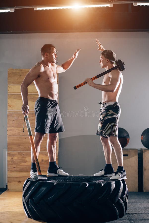 Two Men Doing High Five while Standing on Tire and Holding ...