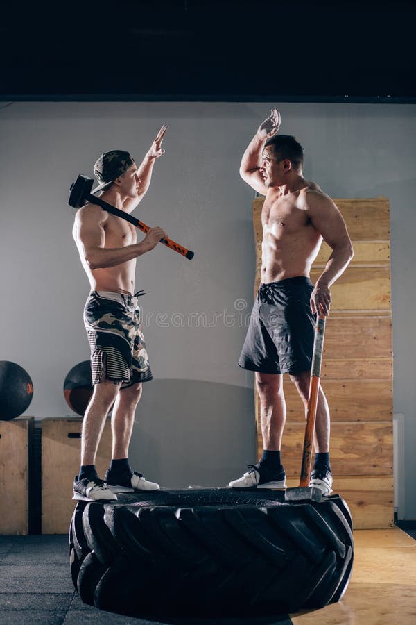 Two Men Doing High Five while Standing on Tire and Holding ...