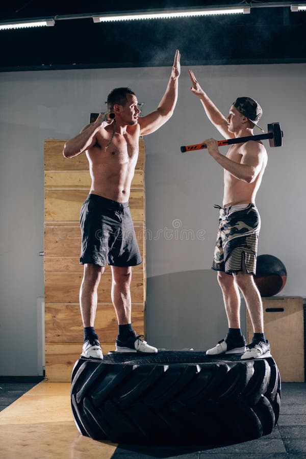 Two Men Doing High Five while Standing on Tire and Holding ...