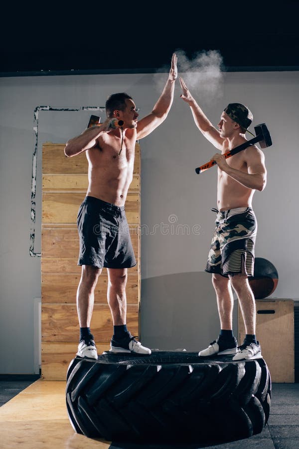 Two Men Doing High Five while Standing on Tire and Holding ...