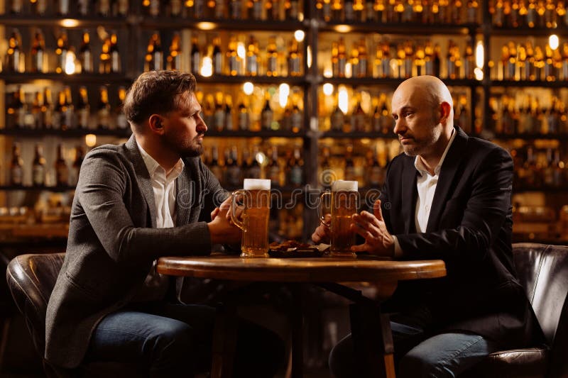 Two Men Engaged in Deep Conversation Over Beer in a Cozy Bar Setting ...