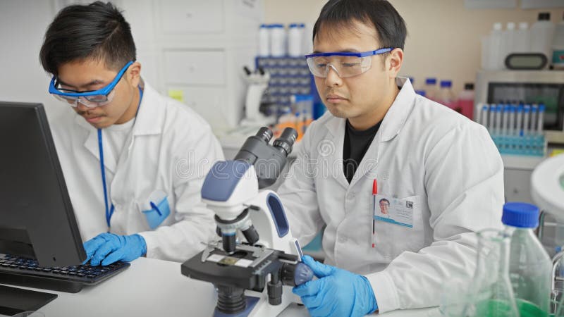 Two Men in Lab Coats Conduct Research with a Microscope and Computer in ...