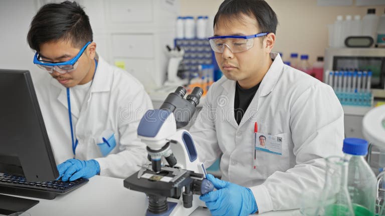 Two Men in Lab Coats Conduct Research with a Microscope and Computer in ...