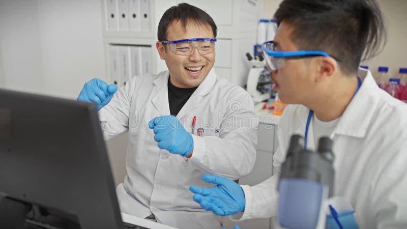 Two Men in Lab Coats and Safety Glasses Work on a Computer in a ...