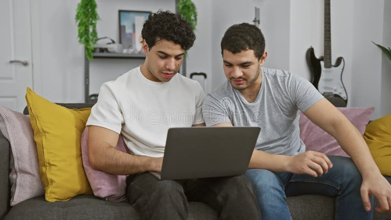 Two Men Looking at a Laptop on a Couch Indoors, Engaged in a Casual ...