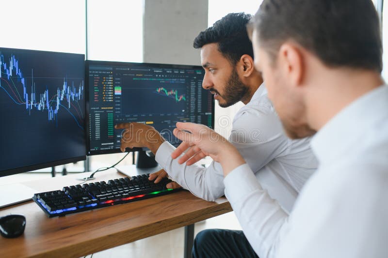 Two Men Traders Sitting at Desk at Office Together Looking at Data ...