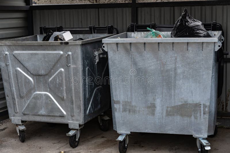 Two Metal Garbage Containers Stand Side by Side, One Filled with a ...