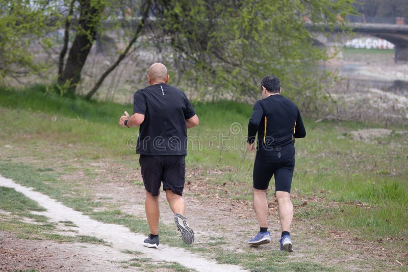 Two Middle-aged Men Jogging Along the Banks of a River and a Bridge in ...