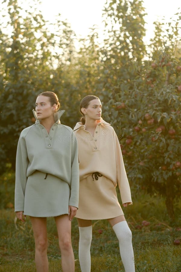 Two Models in Stylish Tracksuits Pose in Apple Orchard at Sunset . the ...