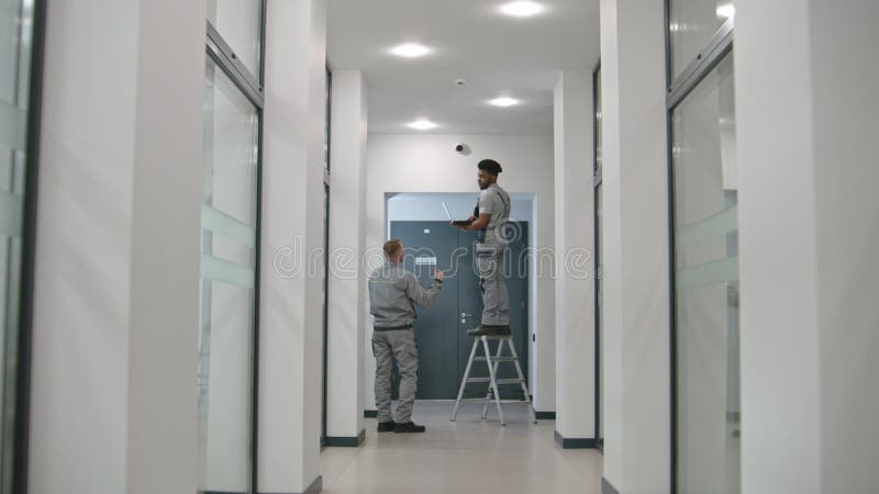 Two Multi Ethnic Installers in Uniform Sets Up Security Camera Stock ...