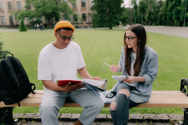Two Multiethnic Students are Sitting on a Bench Near the Campus and ...