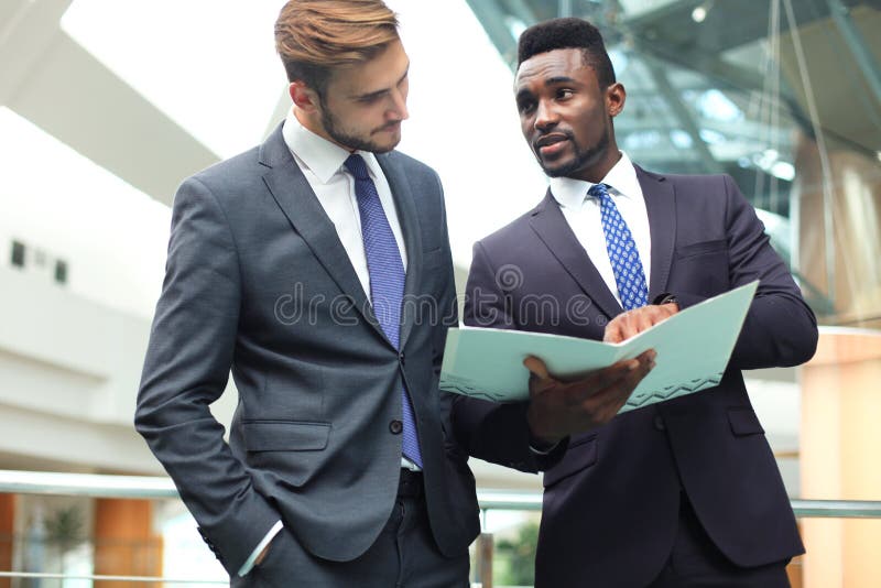 Two Multinational Young Businessmen Discussing Business at Meeting in ... Two Multinational Young Businessmen Discussing Business at Meeting in ...
