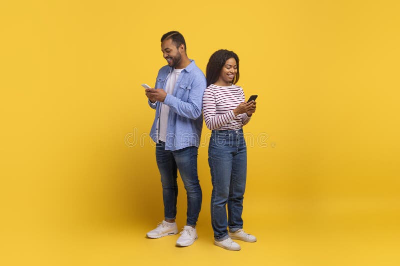 Two People Standing Back To Back Using Smartphones Against A Yellow