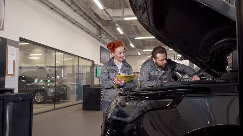 Two Professional Car Mechanics Examining Engine of a Car, Making Notes ...