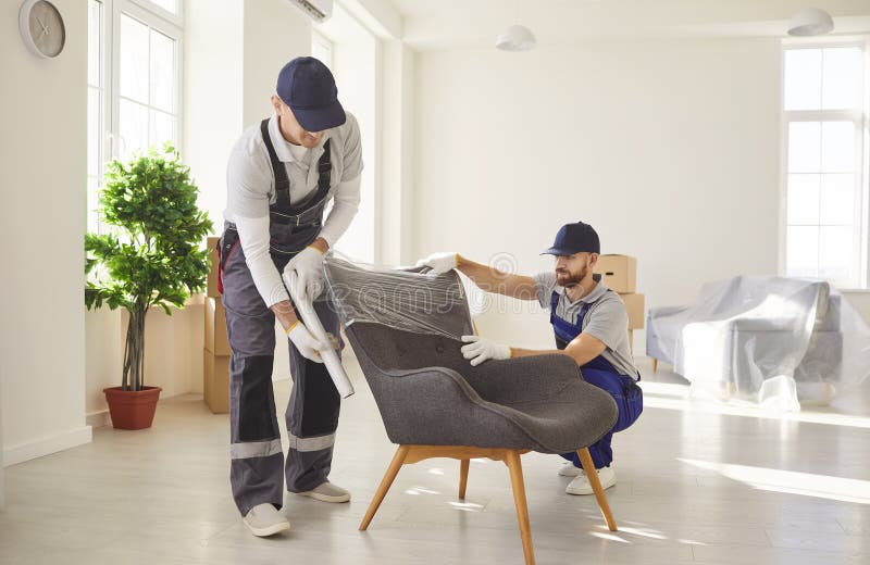 Two Professional Movers in Uniform Unpacking Armchair in Bright Room ...