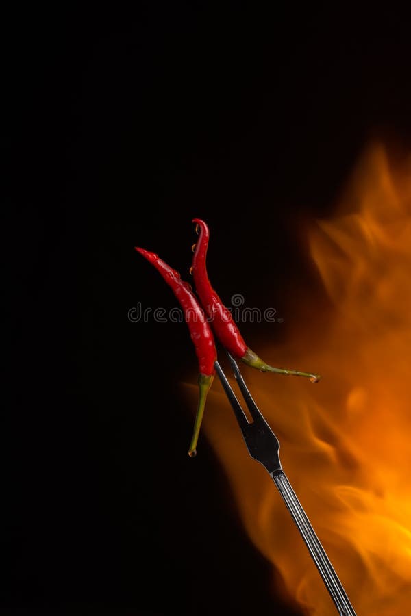 Two Red Chilli Peppers on a Fork with a Flame Behind on a Black ...