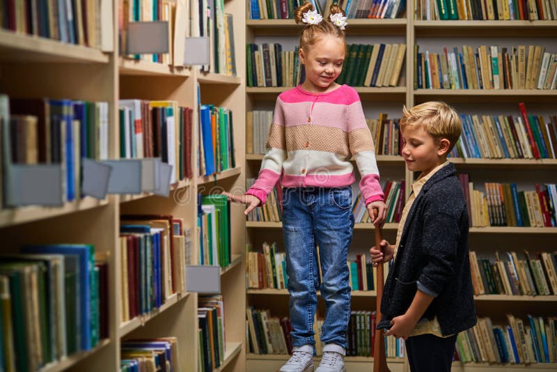 Two School Children Help Each Other To Get a Book from Shelf Stock ...