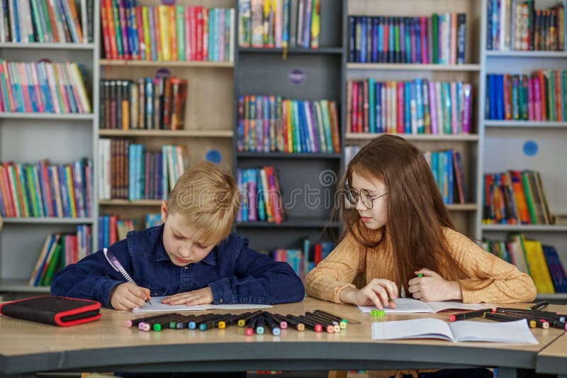 Two Schoolchildren Write and Draw Sitting at Table in Library ...
