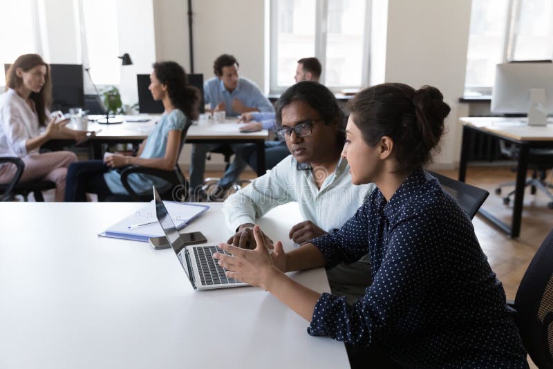 Two Serious Indian Colleagues Talking at Work Table, Sharing Laptop ...