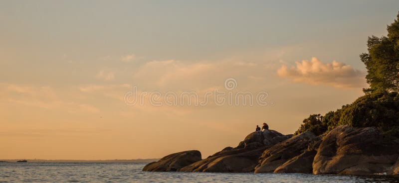 Two Shadows Sitting on a Rock during the a Sunset in Front of the Sea ...