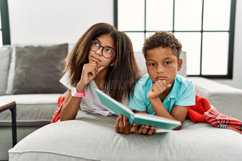 Two Siblings Lying on the Sofa Reading a Book with Hand on Chin ...