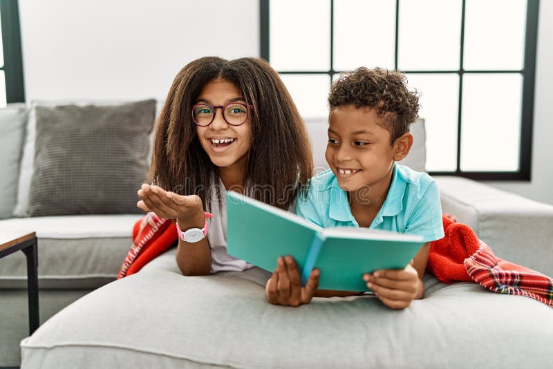 Two Siblings Lying on the Sofa Reading a Book Pointing Aside with Hands ...