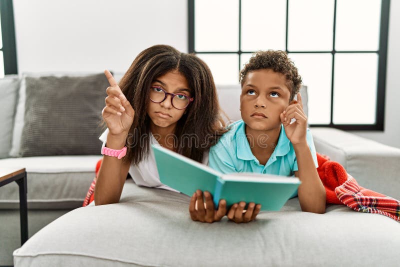 Two Siblings Lying on the Sofa Reading a Book Pointing Up Looking Sad ...