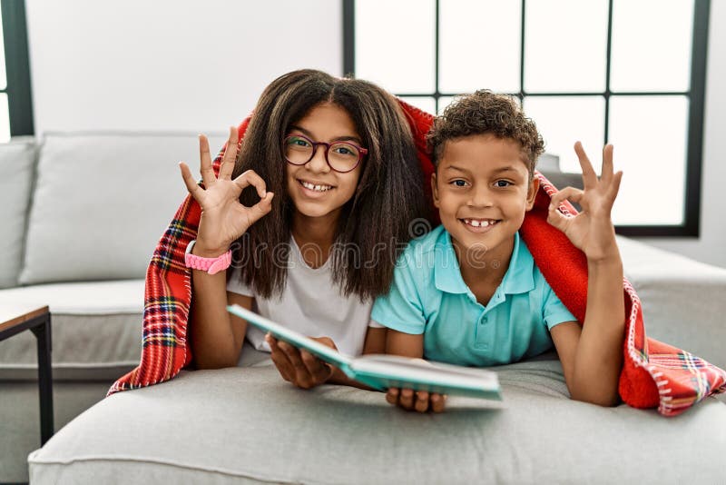 Two Siblings Lying on the Sofa Reading a Book Smiling Positive Doing Ok ...