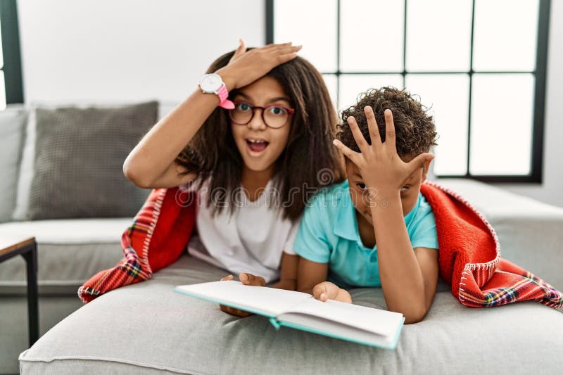 Two Siblings Lying on the Sofa Reading a Book Surprised with Hand on ...