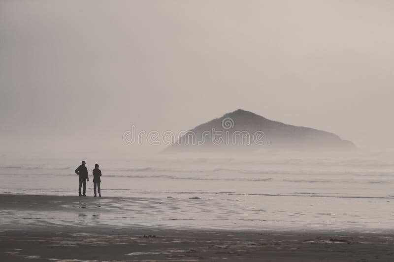 Two Silhouetted People Standing on a Beach Looking Out at a Distant ...
