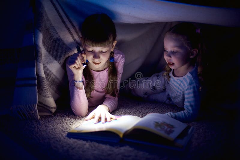 Two Sisters Reading a Book with a Flashlight in a Dark Room at Night ...