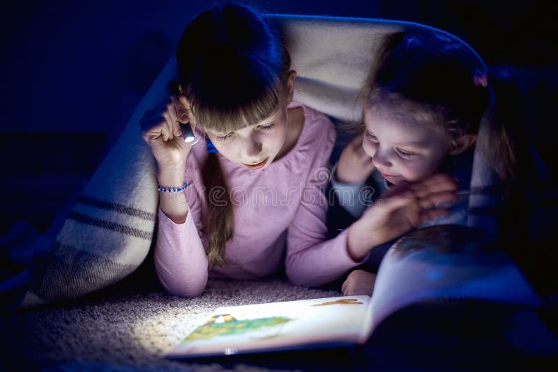 Two Sisters Reading a Book with a Flashlight in a Dark Room at Night ...