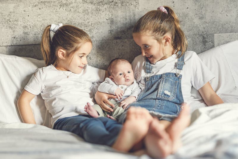 Two Sisters Sit on Bedroom with Newborn Son at Home Stock Photo - Image ...