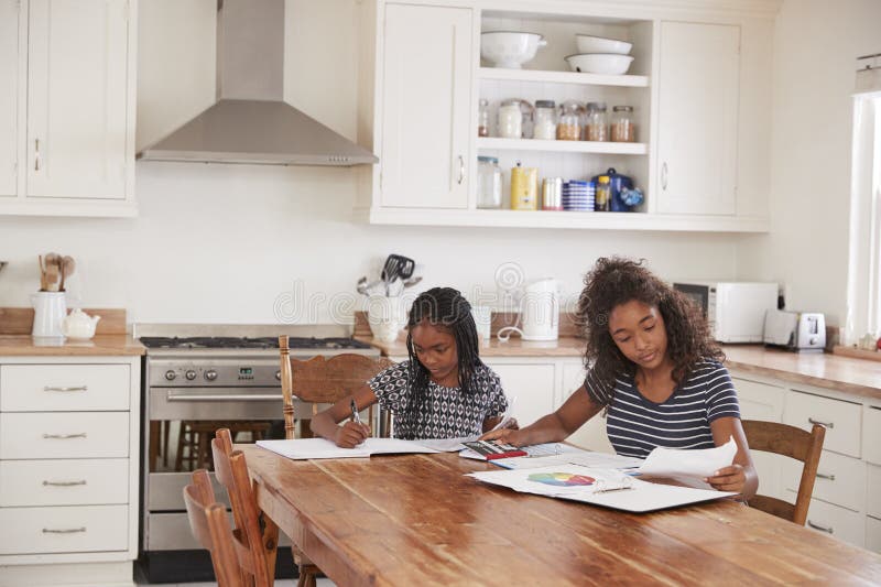 Two Sisters Sitting at Table in Kitchen Doing Homework Stock Photo ...