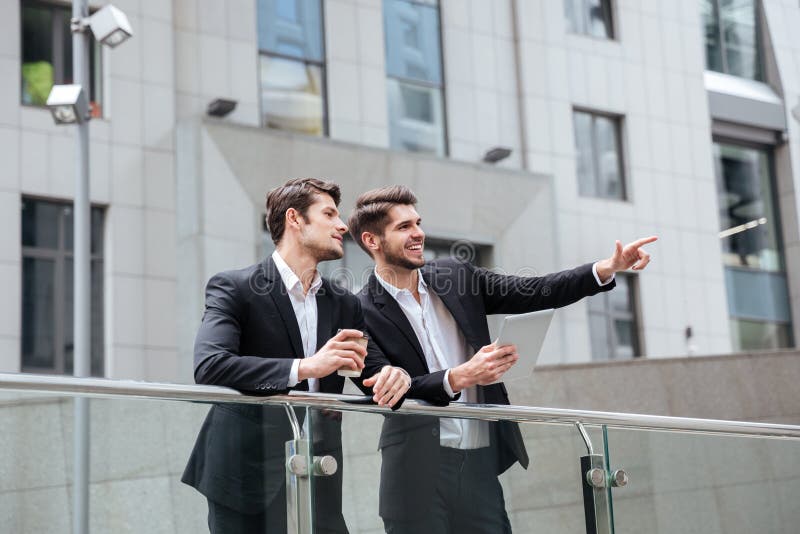 Two Smiling Businessmen Talking and Pointing Away Stock Image - Image ...