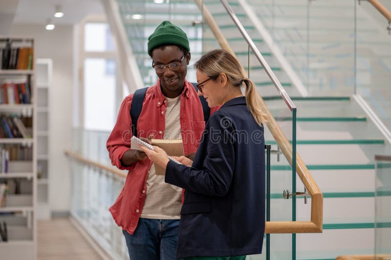 Two Smiling Diverse Students Talking Discussing Homework while Standing ... Two Smiling Diverse Students Talking Discussing Homework while Standing ...