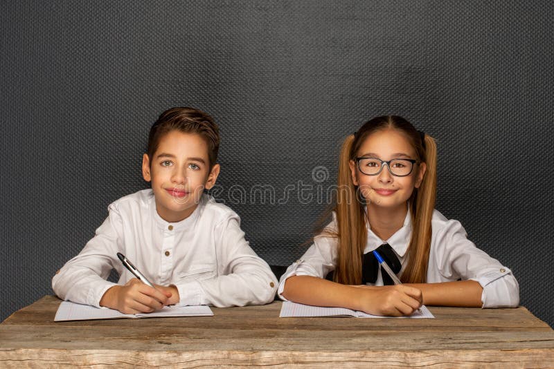 Two Smiling Kids at the Table Write with Pen, on Black Wall Stock Photo ...