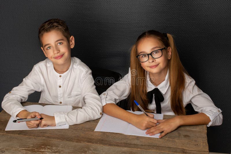 Two Smiling Kids at the Table Write with Pen, on Black Wall Stock Image ...