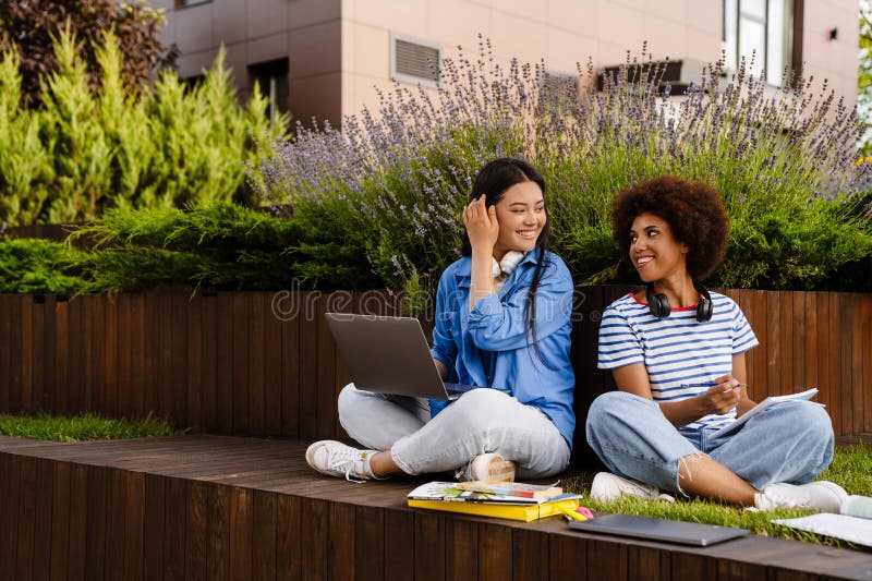 Two Smiling Female Students Using Laptop and Writing Down Notes while ...