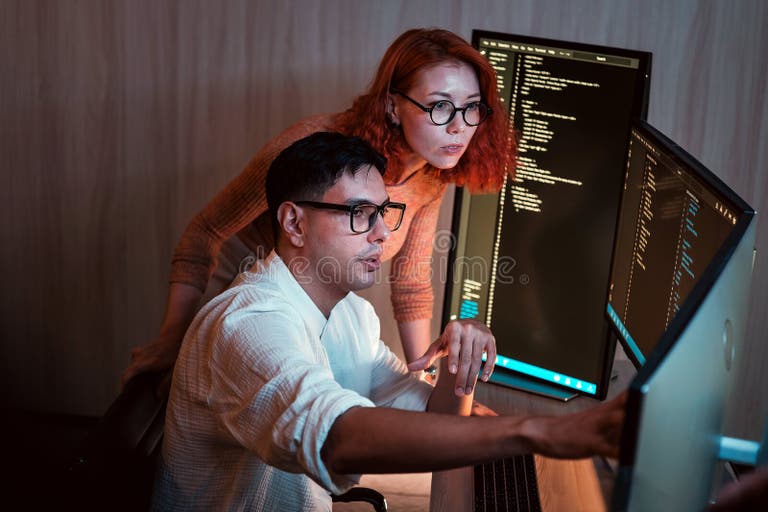 Two Software Developers Collaborate at Dual Monitors in Modern Office at Night. Coding ...