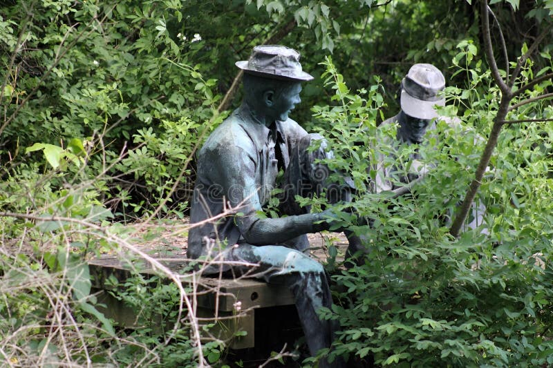 Two Statue Figures Sit in the Middle of Lush Vegetation and Trees ...