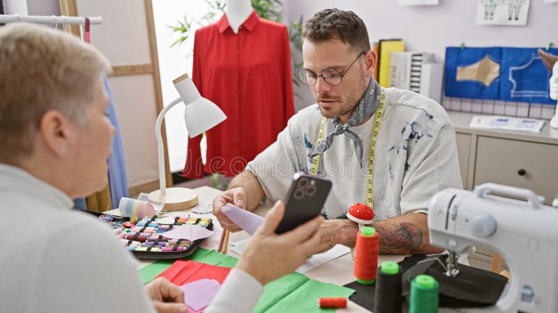 Two Tailors Discussing Designs in a Tailor Shop, with One Holding a ...